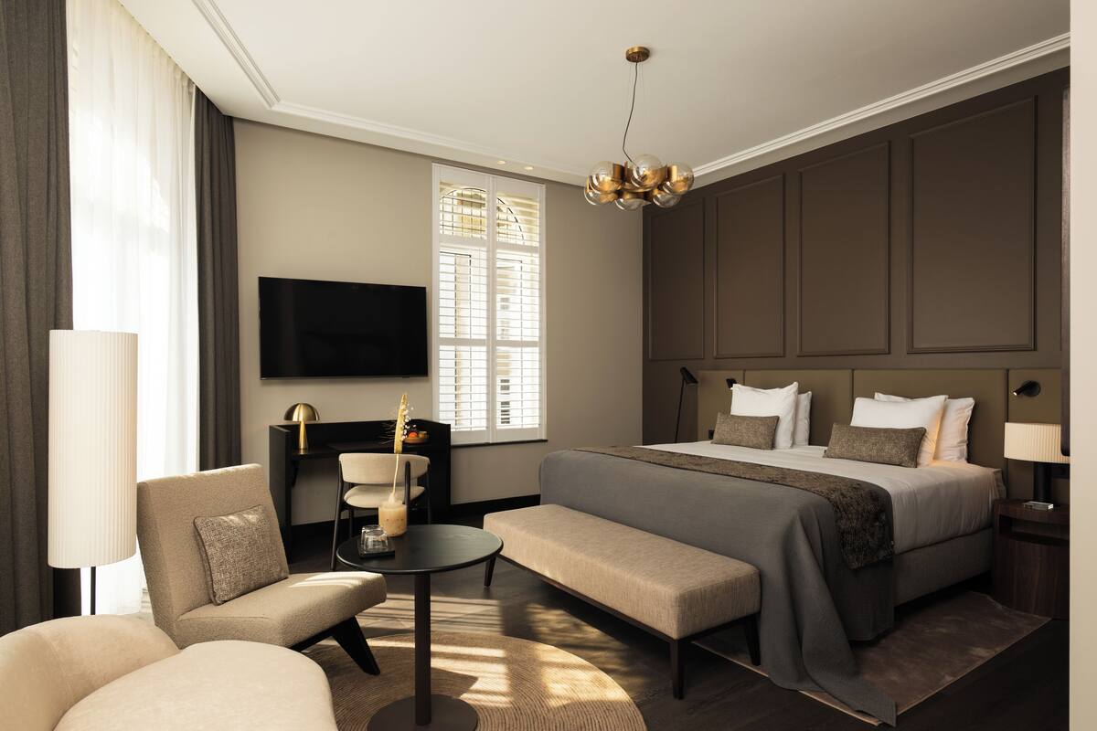 Quarto de hotel moderno com uma cama grande, um sofá, uma escrivaninha e uma televisão.