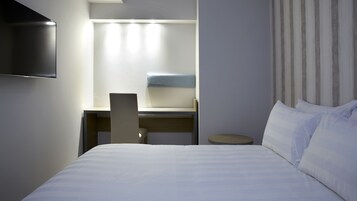 Quarto de hotel com cama, escrivaninha, cadeira e televisão na parede.
