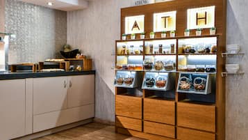 Um balcão de pequeno-almoço com diversos alimentos e uma vitrine de madeira com frascos de acompanhamentos.