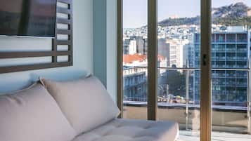 Quarto moderno com sofá, TV fixada em painel de madeira e grande porta de vidro deslizante com vista para a cidade.