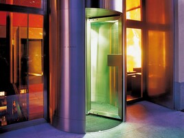 Um elevador moderno com acabamento metálico e porta de vidro, localizado no saguão de um hotel.