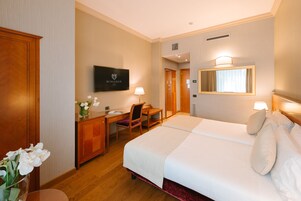 Quarto de hotel com cama, escrivaninha, cadeira, televisão e espelho.