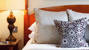 Uma cama bem arrumada com almofadas estampadas e cabeceira de madeira, uma luminária de cabeceira e uma mesinha de apoio com um controle remoto.