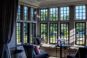 Um quarto com amplas janelas, um banco e uma pequena mesa com flores.
