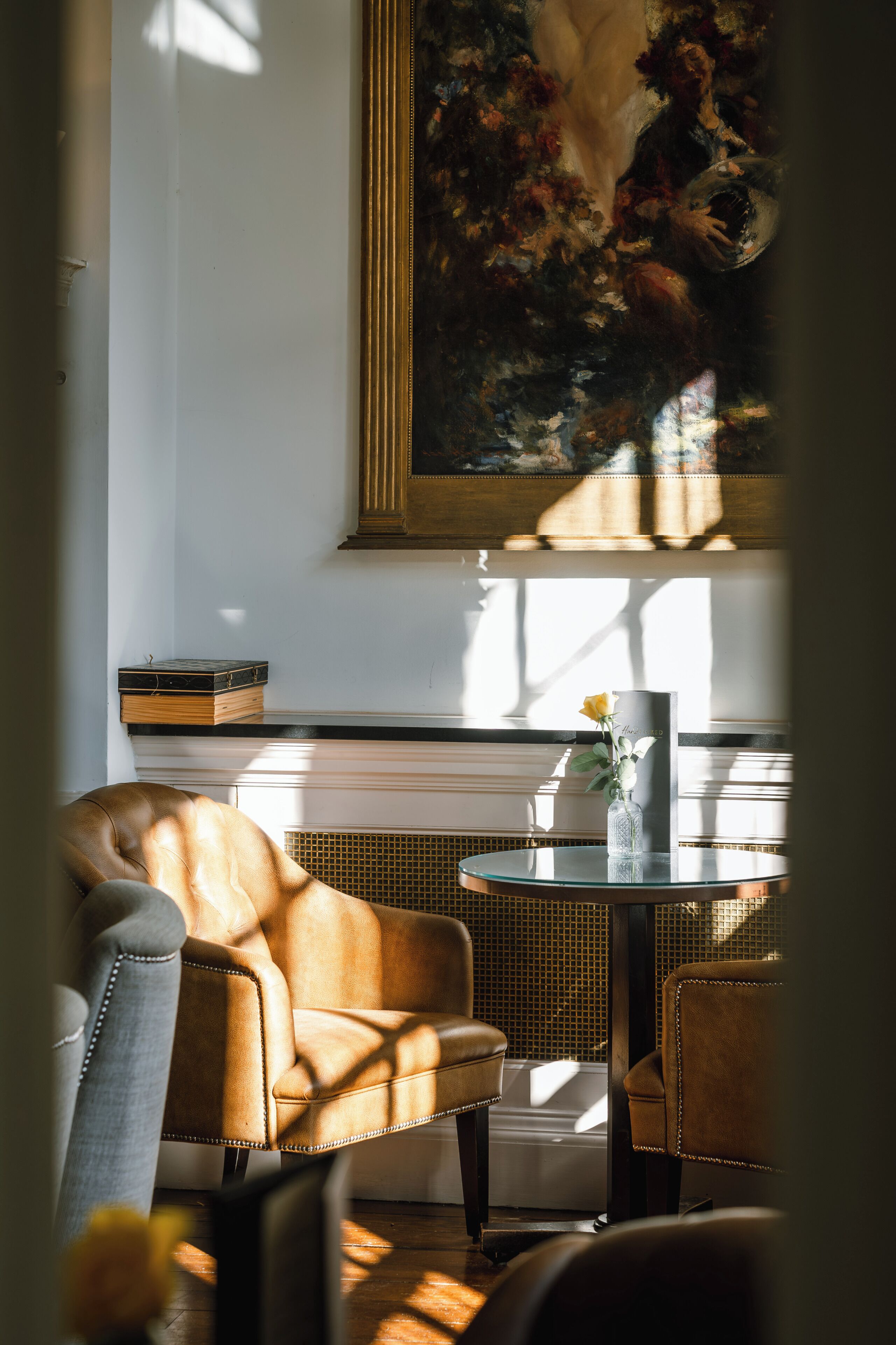 Um quarto com uma mesa redonda, duas cadeiras, um vaso com uma única flor e um quadro grande na parede.