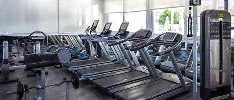 Academia com esteiras, aparelhos de musculação e uma grande janela.