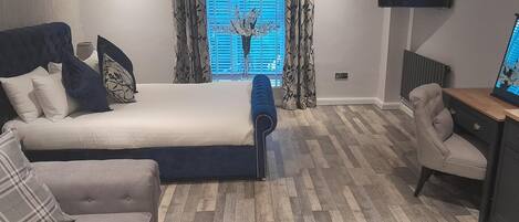 Quarto com cama, sofá, escrivaninha e televisão.