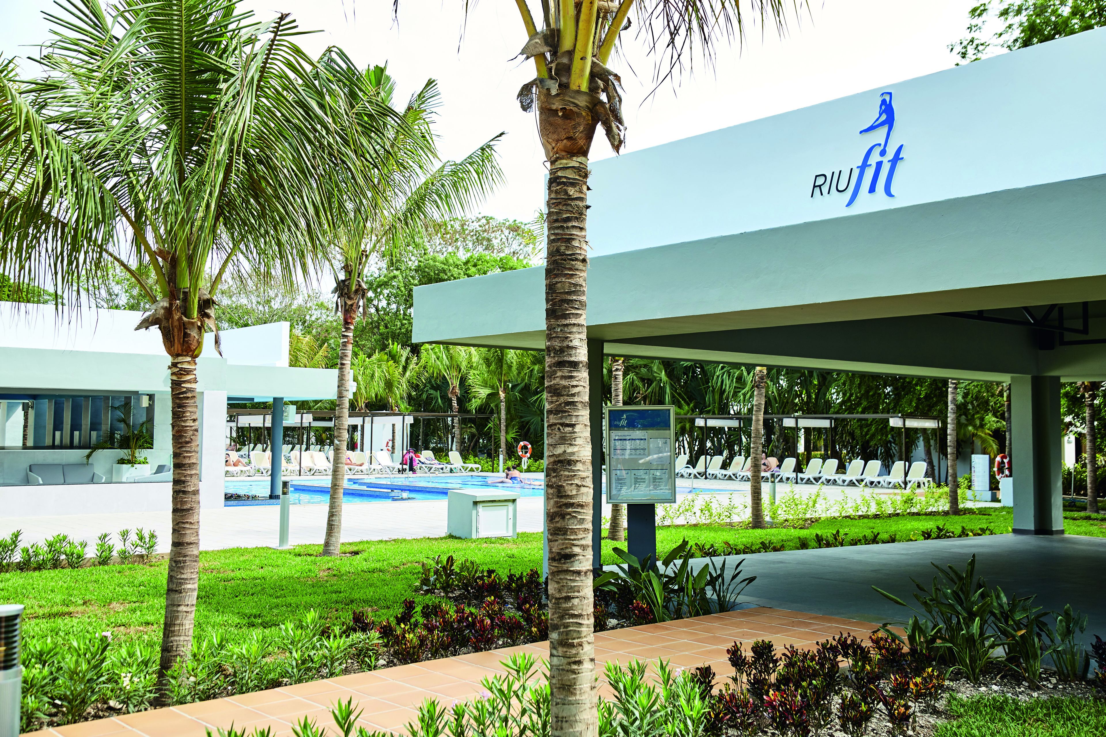 Um hotel moderno com área de piscina, palmeiras e um espaço de estar coberto.