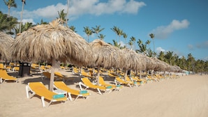 Uma praia com fileiras de cadeiras de praia amarelas e guarda-sóis de palha.