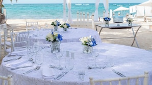 Montagem de casamento na praia, com mesa redonda, cadeiras brancas e um toldo branco.