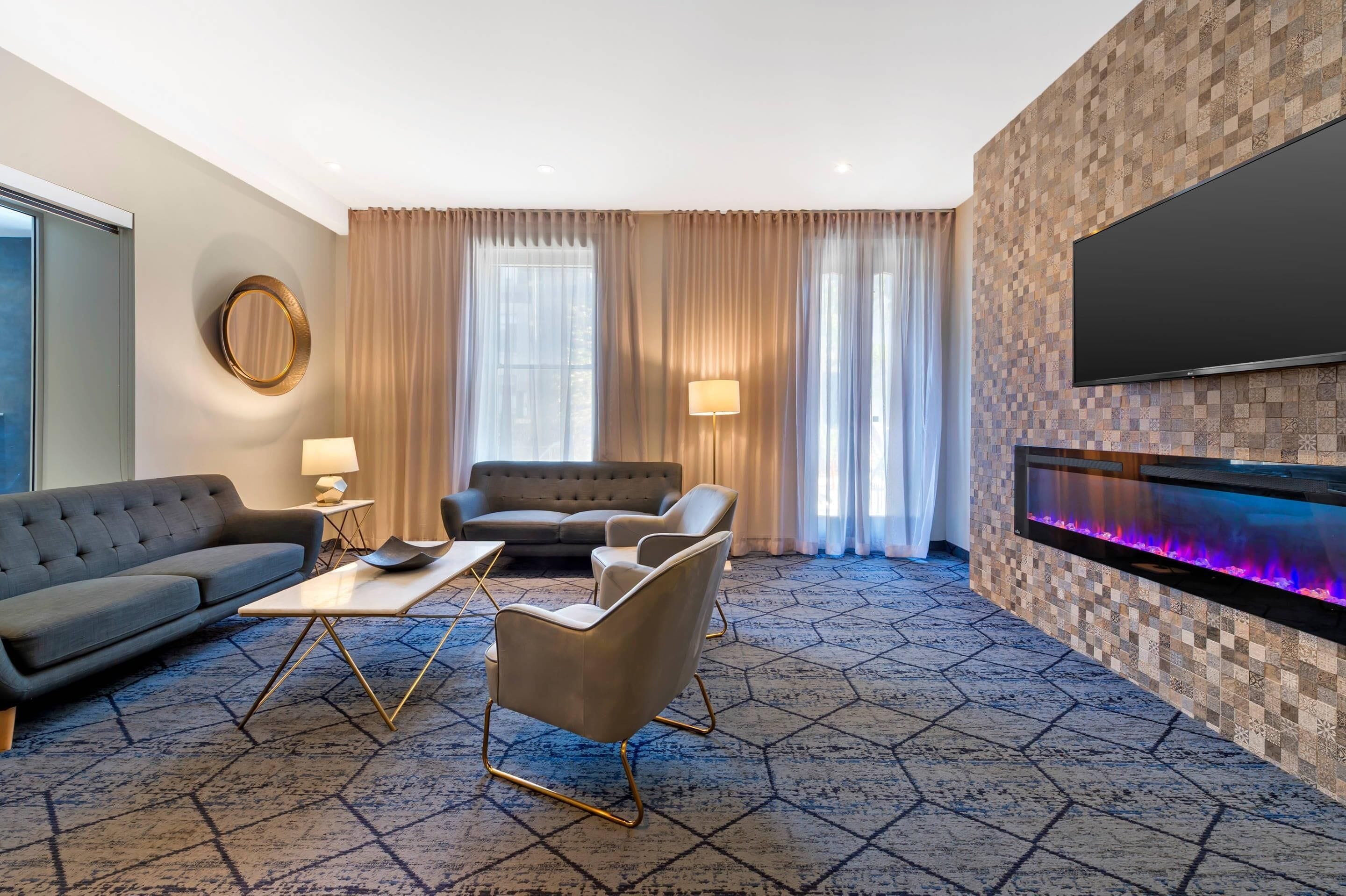 Quarto de hotel moderno com sofá, poltrona e televisão de tela plana fixada na parede.