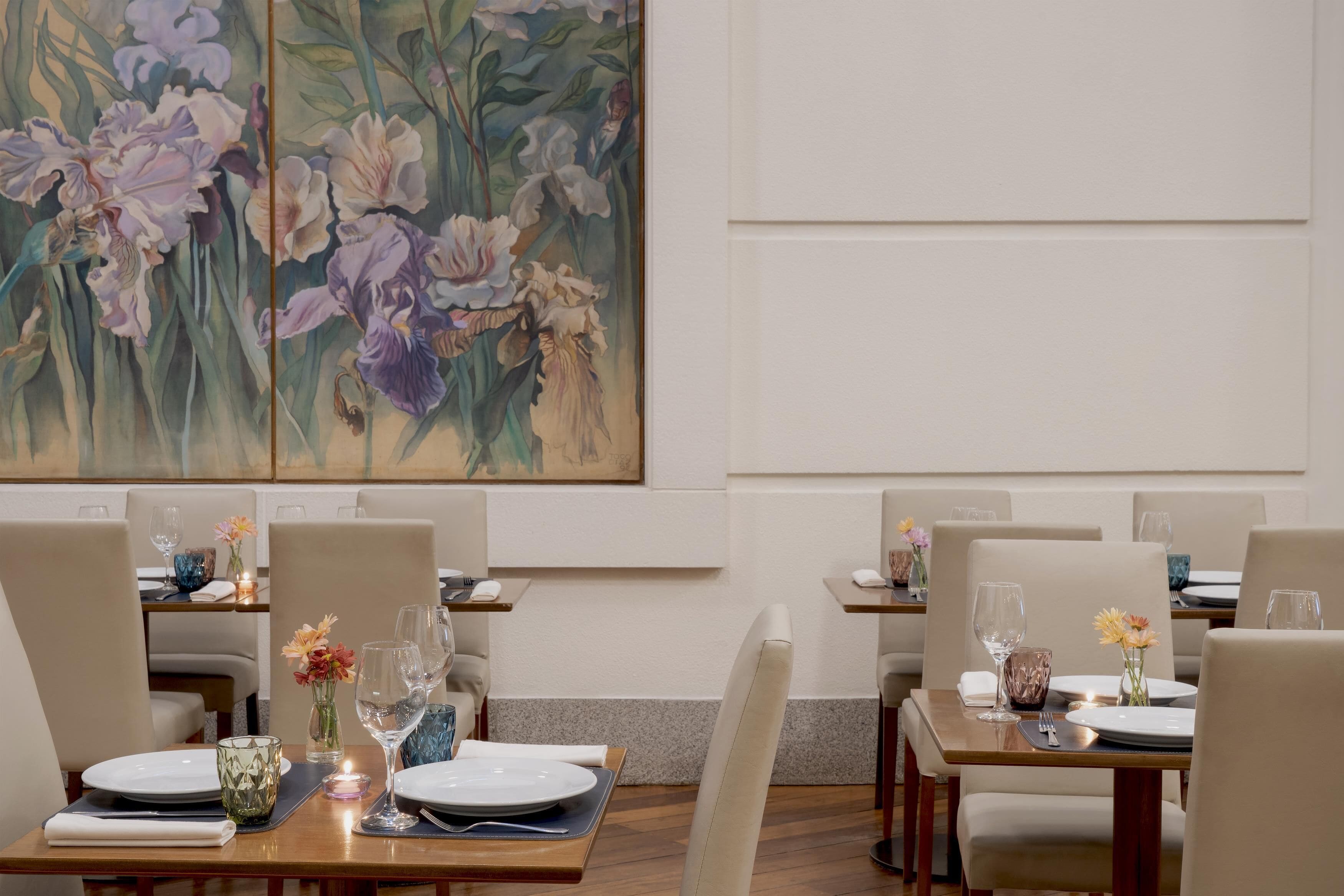 Um restaurante com mesas montadas para refeições, cadeiras e uma grande pintura floral na parede.
