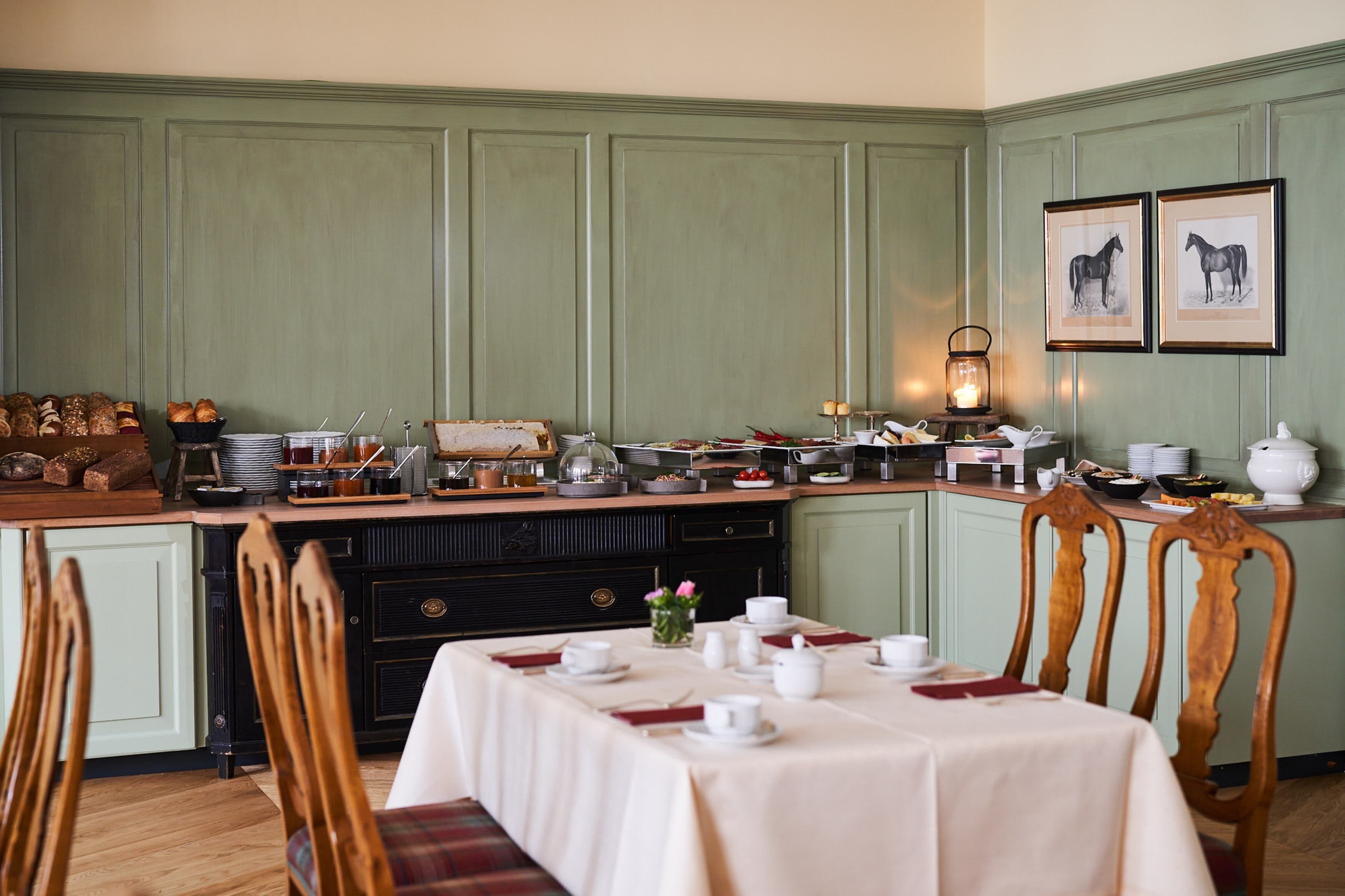 Uma sala de jantar com uma mesa posta para quatro pessoas, um buffet com diversos alimentos e uma vela sobre a mesa.