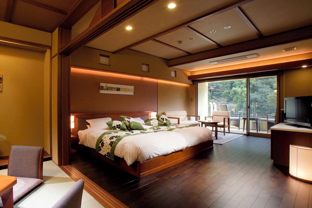 Quarto de hotel com uma cama grande, televisão, escrivaninha e varanda com vista.