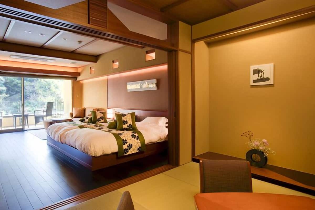 Quarto de hotel moderno com uma cama grande, TV, varanda e uma mesinha com um vaso.