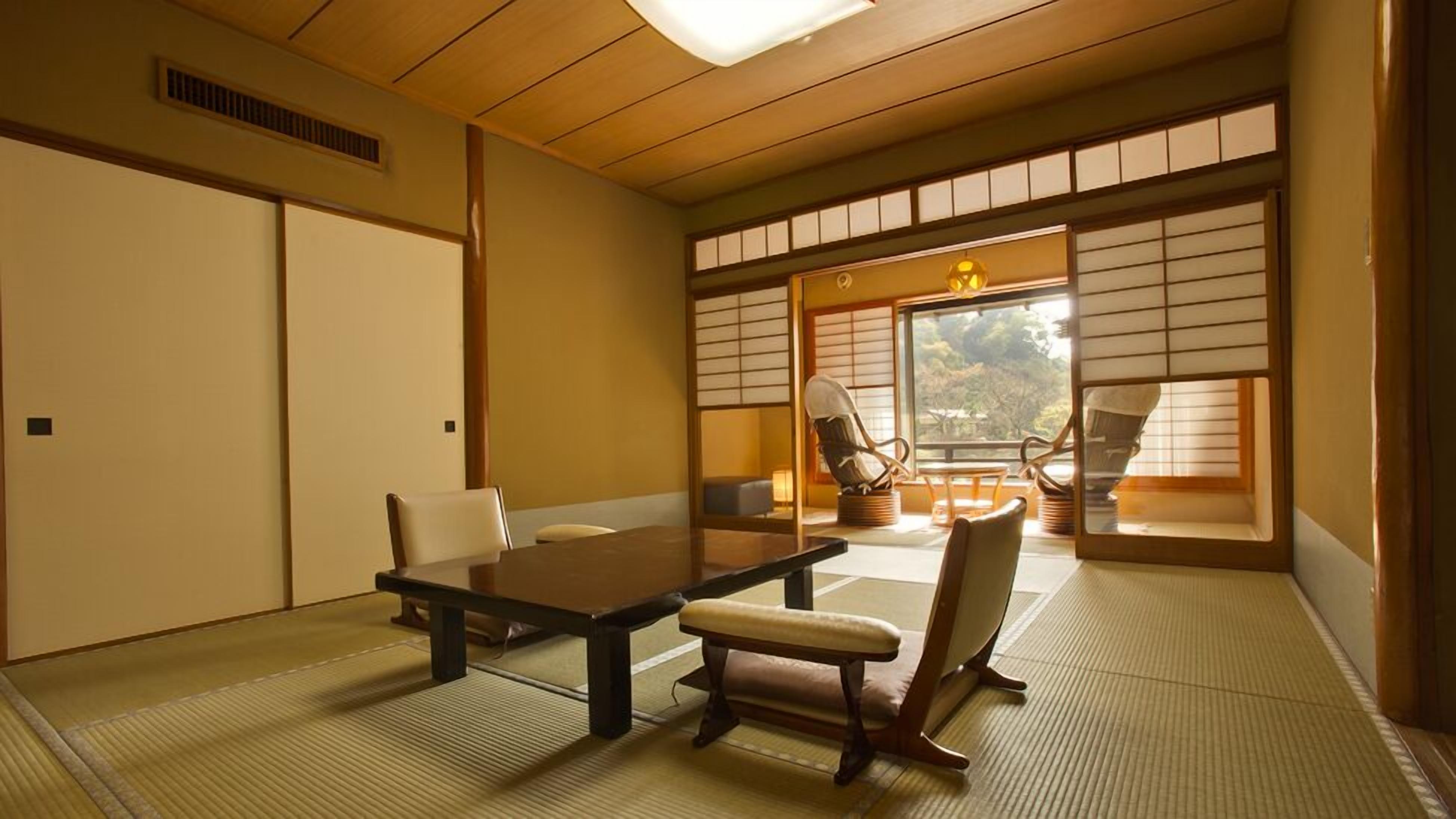 Um quarto japonês tradicional com tatames, uma mesa baixa, cadeiras e portas deslizantes.