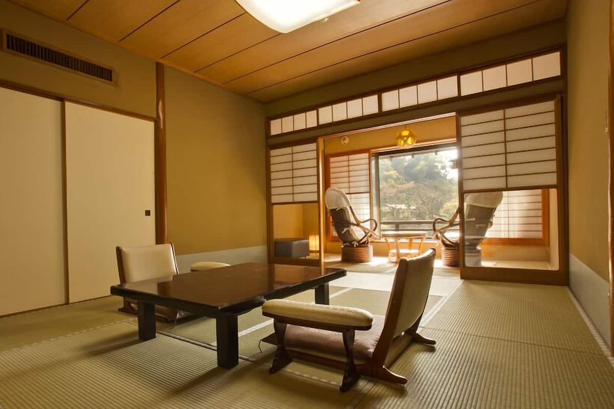 Um quarto japonês tradicional com tatames, uma mesa baixa, cadeiras e portas deslizantes.