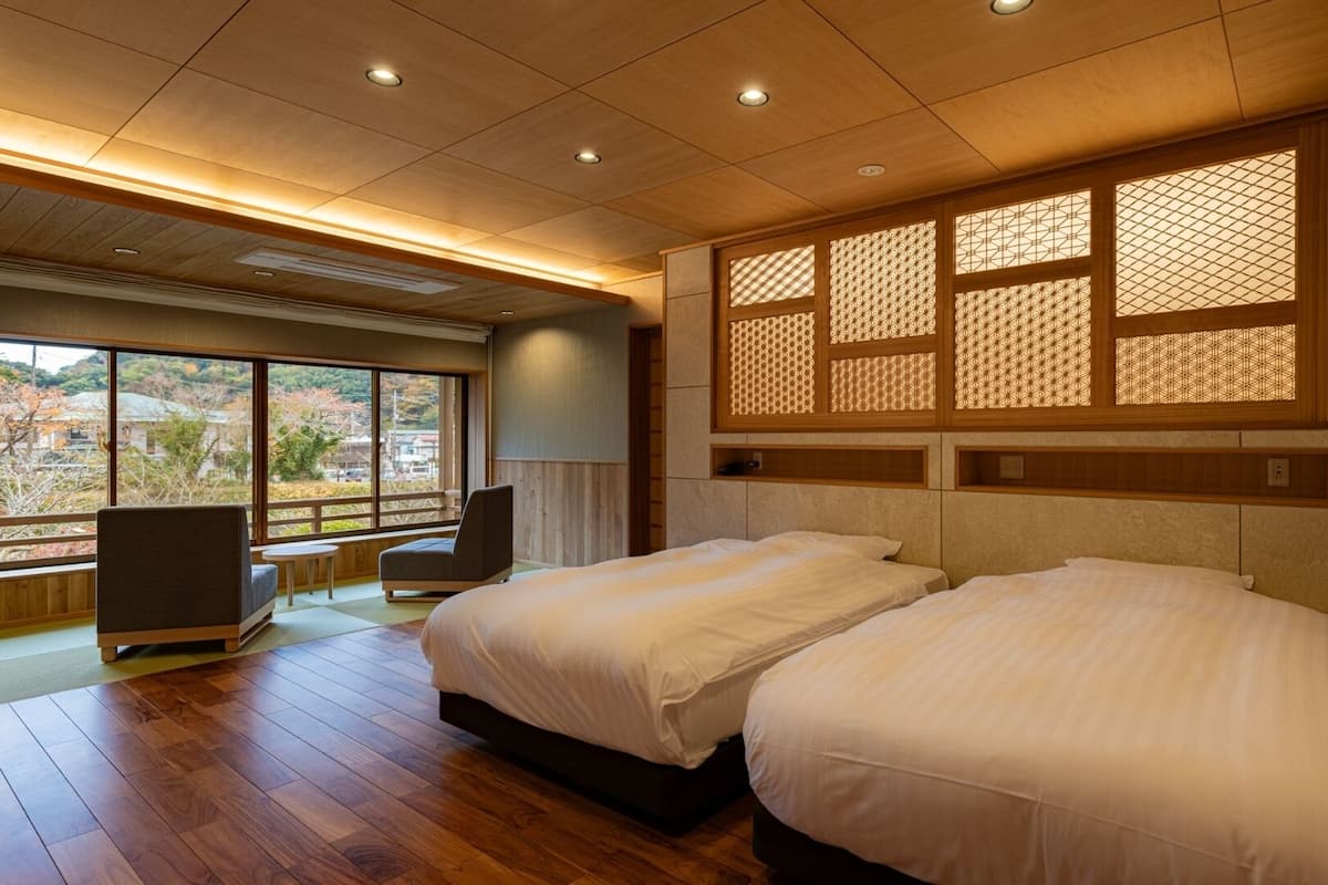Quarto de hotel com duas camas, vista para o exterior e um separador tradicional no estilo japonês.