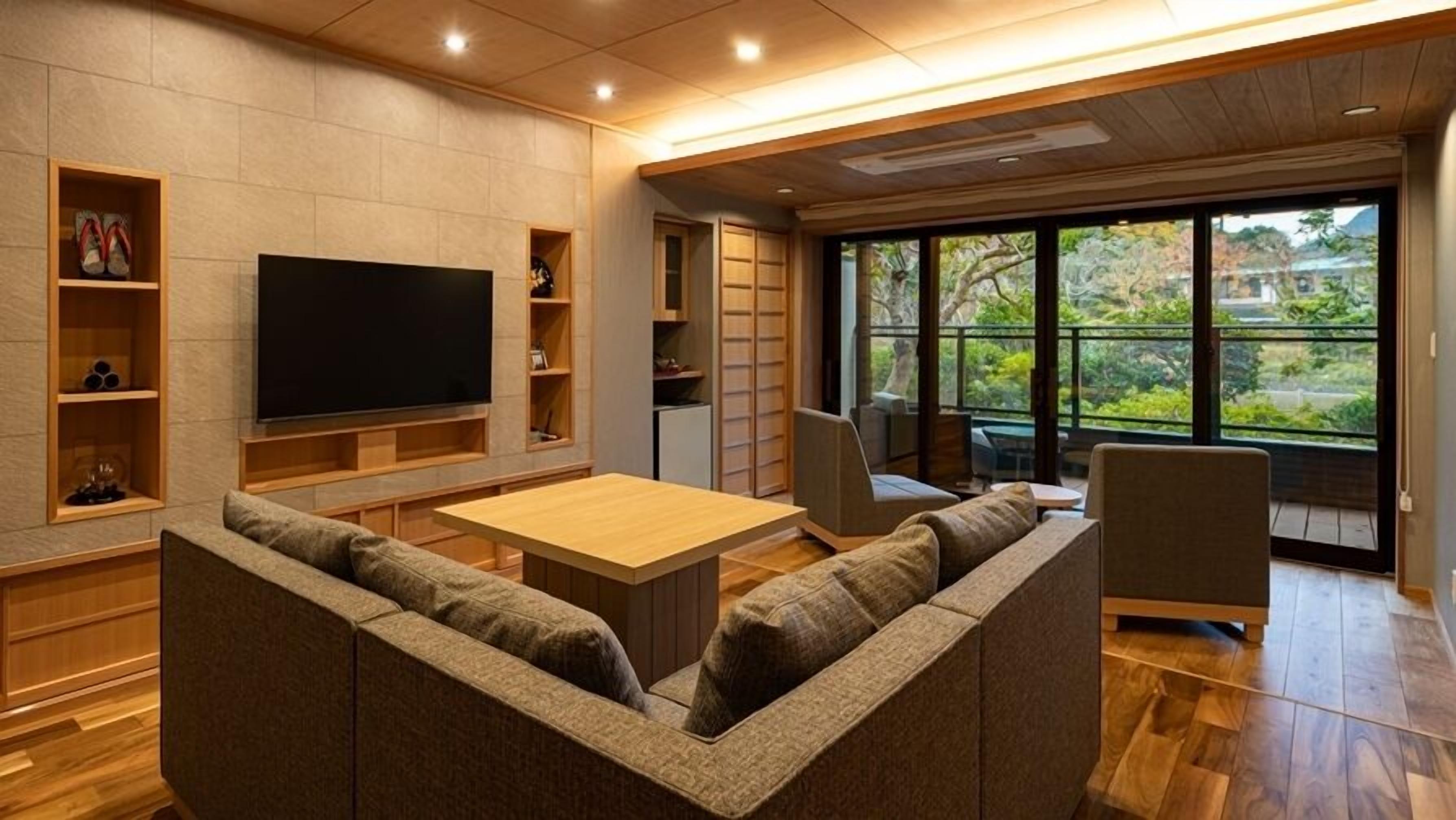 Uma sala de estar moderna com uma televisão de tela plana, prateleiras embutidas, uma mesa de centro de madeira e uma grande janela com vista para áreas verdes.