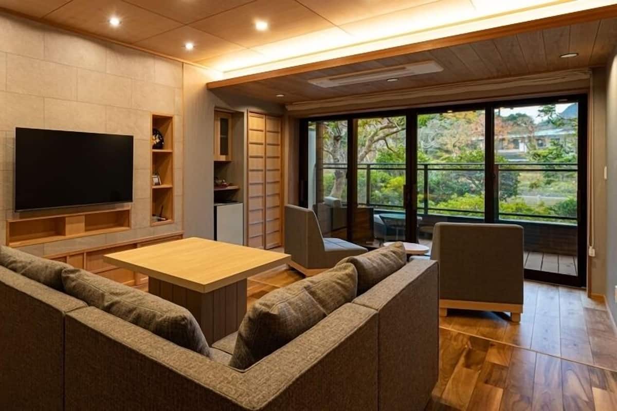 Uma sala de estar moderna com uma televisão de tela plana, prateleiras embutidas, uma mesa de centro de madeira e uma grande janela com vista para áreas verdes.