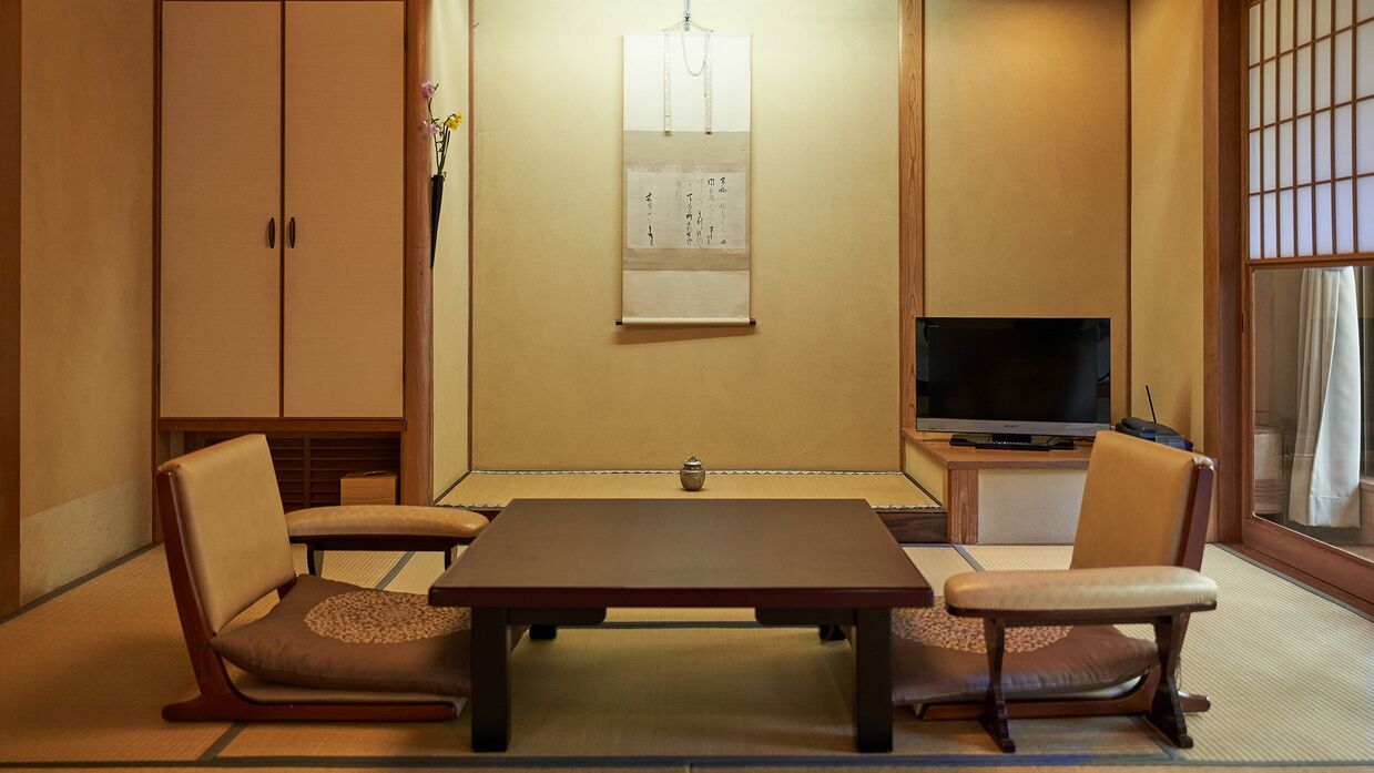 Um quarto japonês tradicional com tatames, uma mesa baixa e duas cadeiras.