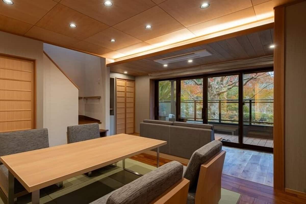 Um interior moderno com uma mesa e cadeiras de madeira, uma escada e uma grande janela com vista para árvores.
