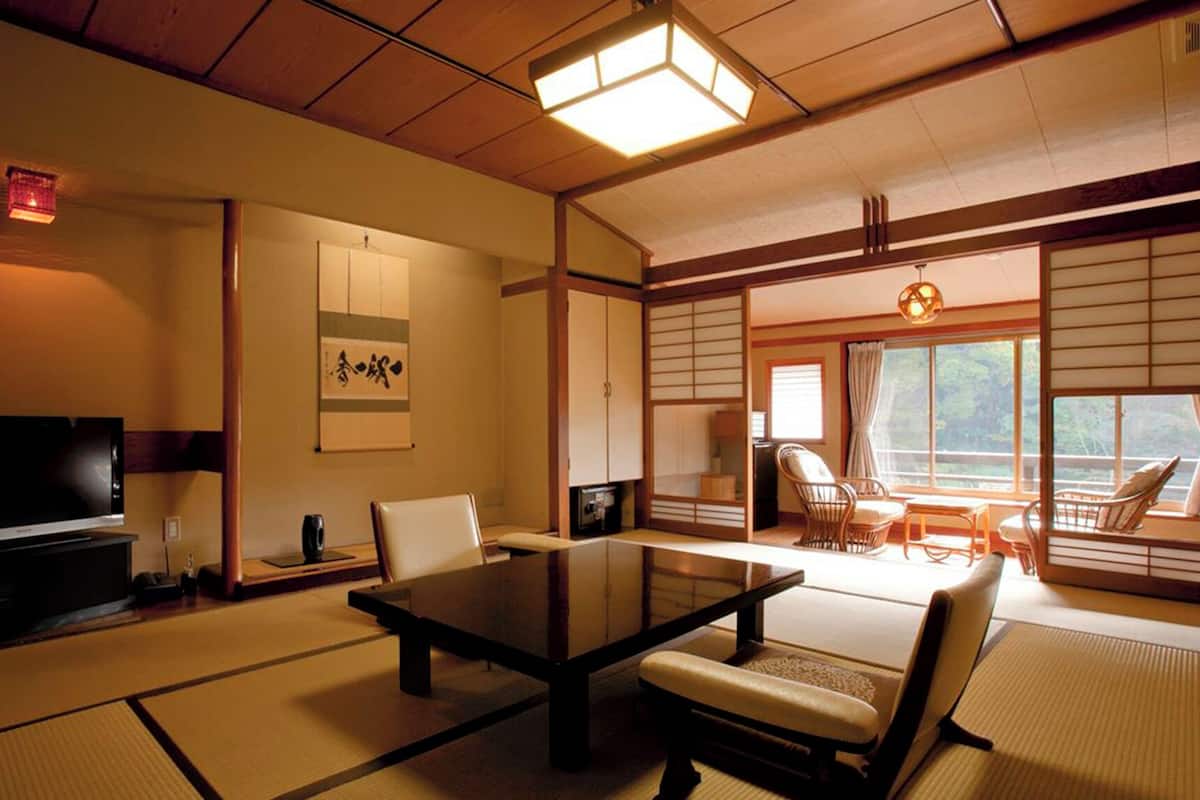 Um quarto em estilo japonês tradicional, com tatames, uma mesa baixa, cadeiras, televisão e portas deslizantes.