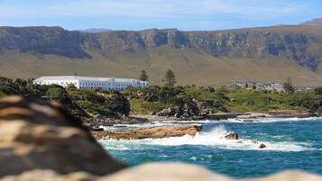 Um hotel à beira-mar com um edifício branco, costa rochosa e montanhas ao fundo.
