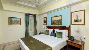 Quarto de hotel com uma cama grande, mesa de cabeceira com luminária, criado-mudo e quadros nas paredes.