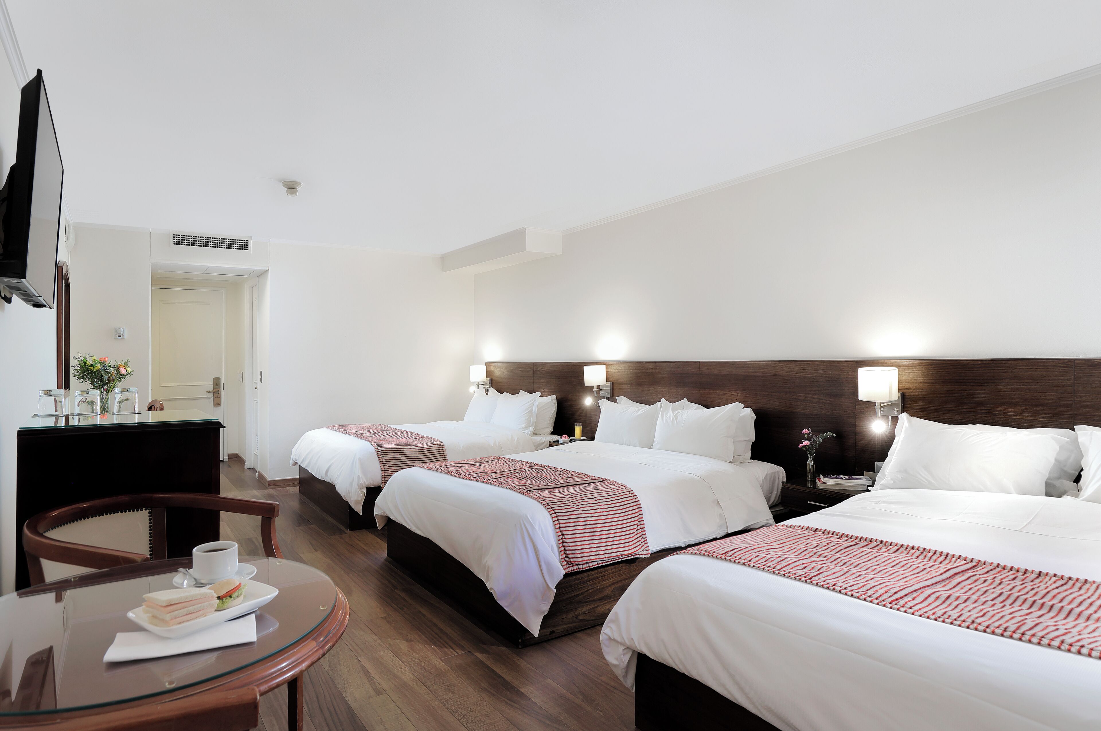Quarto de hotel com duas camas, uma escrivaninha com cadeira, televisão e uma mesa de jantar com um prato de comida.