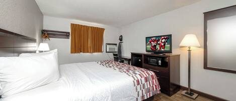Quarto de hotel com cama, TV de tela plana, escrivaninha com computador, luminária e janela com cortinas.