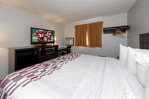 Quarto de hotel com cama, televisão, escrivaninha e ar-condicionado fixado na parede.