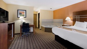 Quarto de hotel com cama, escrivaninha, cadeira, televisão, luminária e banheiro com banheira.