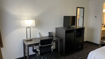 Quarto de hotel com escrivaninha, cadeira, abajur, telefone, televisão e minibar.