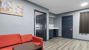 Quarto com sofá vermelho, mesa de madeira, área de cozinha com armários e porta com puxador vermelho.