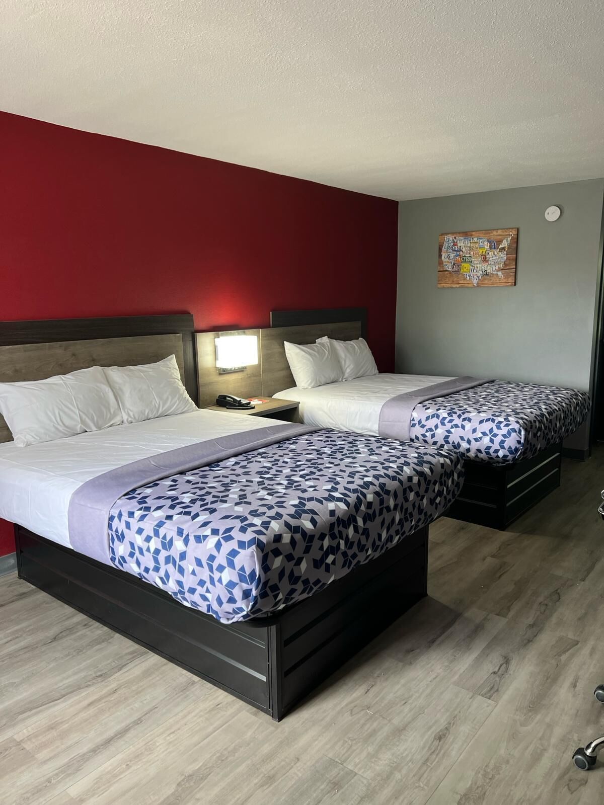 Quarto de hotel com duas camas, parede vermelha, obra de arte com um mapa e piso de madeira.