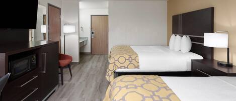 Quarto de hotel com cama, televisão, escrivaninha com abajur e micro-ondas.