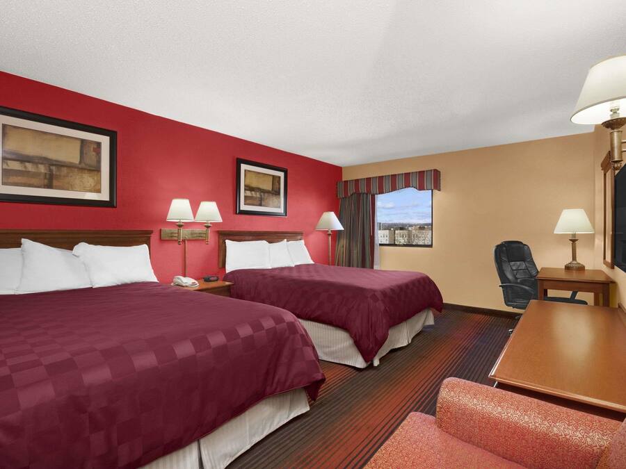 Quarto de hotel com duas camas, uma escrivaninha, uma cadeira e uma janela com vista para a cidade.