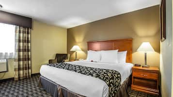 Quarto de hotel com uma cama grande, duas mesas de cabeceira com luminárias, uma cadeira e uma janela com cortinas.