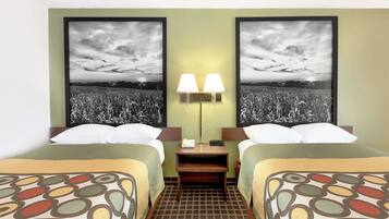 Quarto de hotel com duas camas, uma mesa de cabeceira, uma luminária e duas fotografias emolduradas na parede.