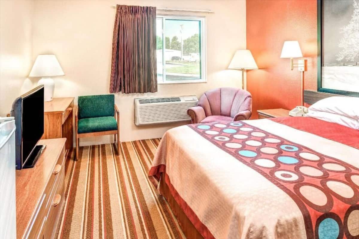 Quarto de hotel com uma cama, duas cadeiras, uma televisão, um ar condicionado e duas lâmpadas.