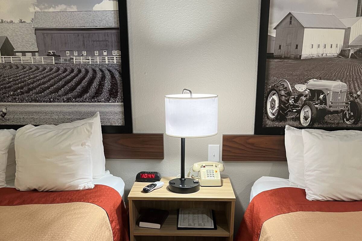 Quarto de hotel com duas camas, mesa de cabeceira com abajur, relógio e telefone.