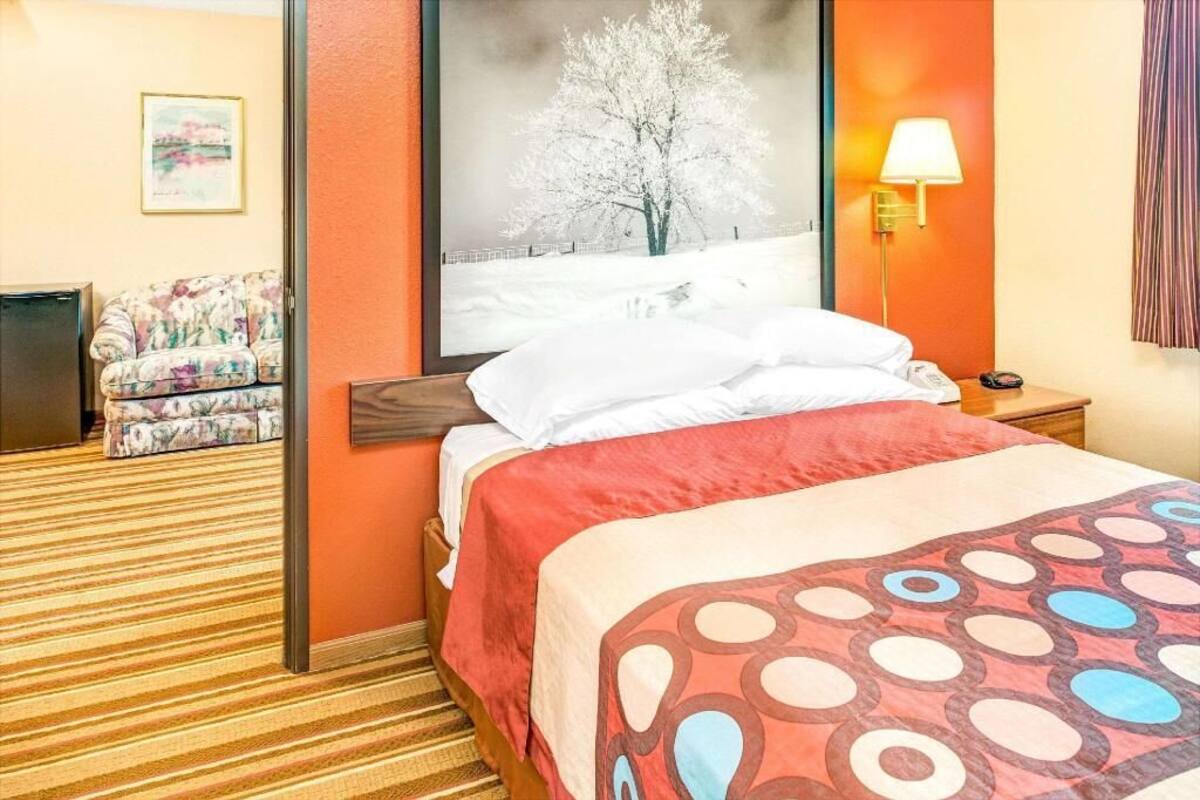 Quarto de hotel com cama, cadeira, luminária e um quadro na parede.