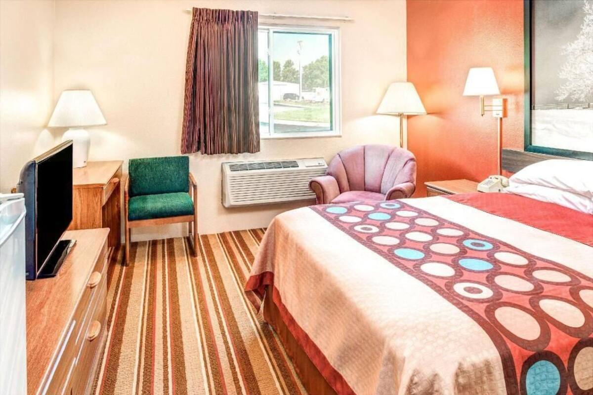 Quarto de hotel com uma cama, duas cadeiras, uma televisão, um ar condicionado e duas lâmpadas.