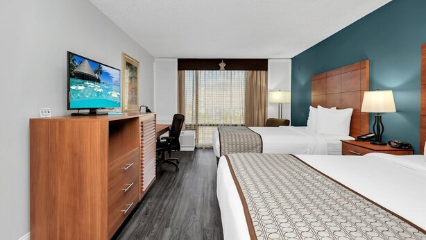 Quarto de hotel com cama, escrivaninha, cadeira, televisão e vista para o mar pela janela.