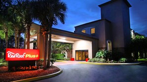 Um hotel Red Roof Plus com design moderno, apresentando uma entrada imponente, áreas verdes bem cuidadas e fachada bem iluminada.
