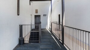 Um corredor estreito com corrimão de metal, uma lixeira e uma porta com uma placa em cima.