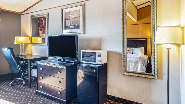 Quarto de hotel com escrivaninha, televisão, micro-ondas, cómoda, cadeira e um espelho grande.