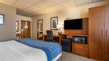 Quarto de hotel com uma cama grande, uma escrivaninha com cadeira, televisão, micro-ondas e armários de madeira.