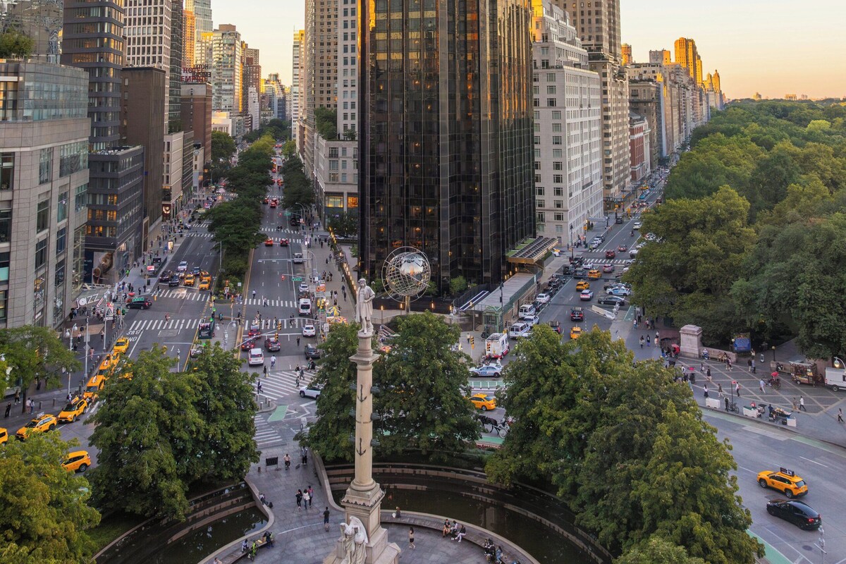 Paisagem urbana com um arranha-céu imponente, um monumento central e edifícios ao redor.